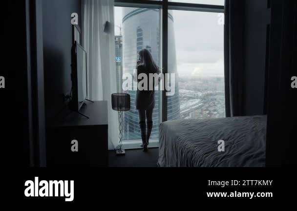 Rear view at Beautiful blonde woman standing looking out of full-length ...