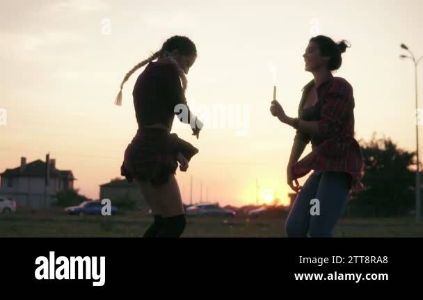 Two attractive girlfriends dancing together and waving with firework ...