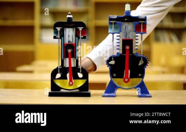 Man rotates each of two models of internal combustion engine on desk ...