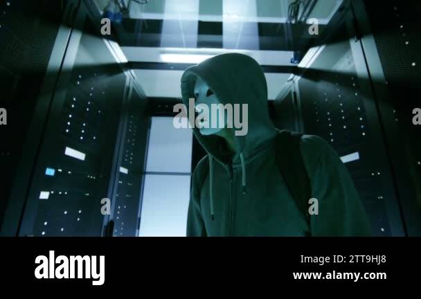 Masked Hacker in a Hoodie Walks Through Corporate Data Center with Rows ...