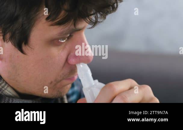 Sick man inhaling through inhaler nozzle for nose. Close-up face, side ...