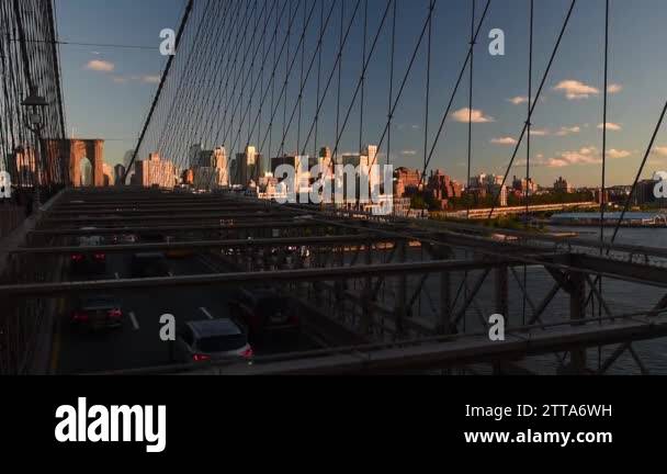 Cars riding and pedestrians walk over the Brooklyn Bridge at sunset ...