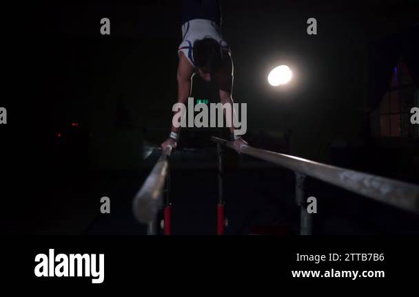 Male gymnast acrobat performs handstand on parallel bars in a dark room ...