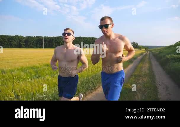 Two muscular men running and talking outdoors. Young athletic guys ...