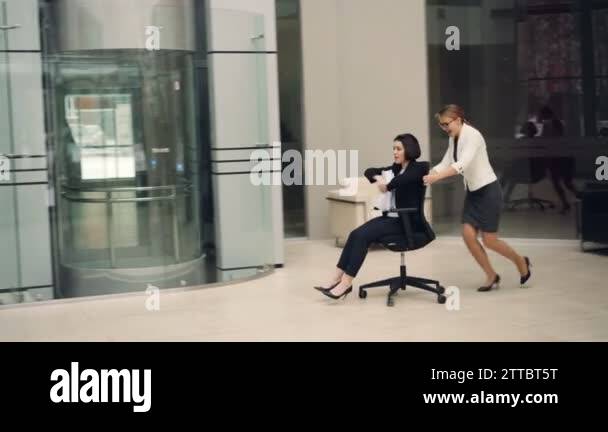 Playful girls businesswomen are having fun in office lobby riding ...