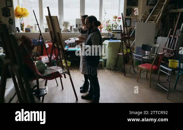 Skilled artist man teaching young girl to draw paintings and explaining ...