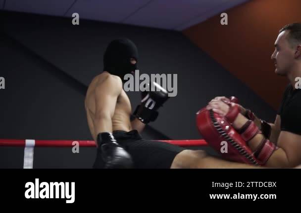 A professional boxer and his coach work on the boxing paws in the ring ...