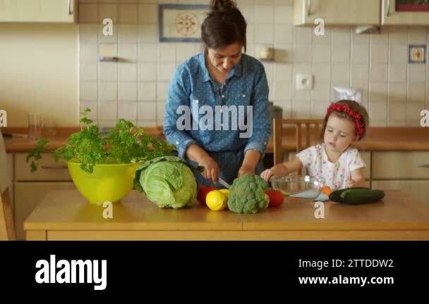 A young mother is preparing dinner in the kitchen. She cuts the carrots ...