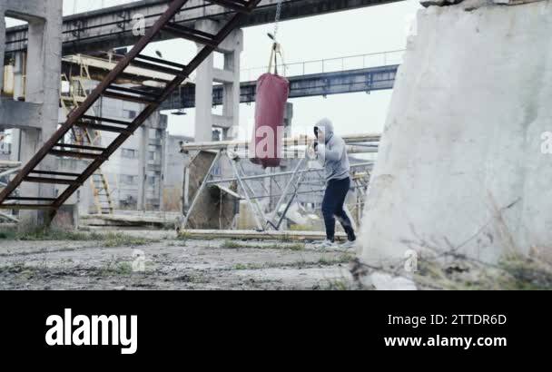 Far shot of the young handsome boxer with a beard kicking a red bag in ...
