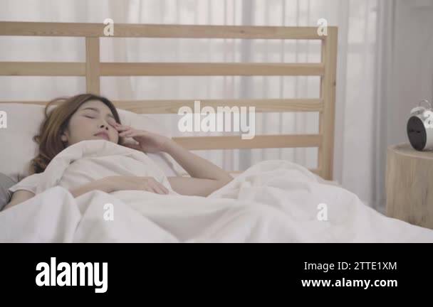 Beautiful attractive young Asian woman wake up, smiling and stretching her arms in her bed in ...