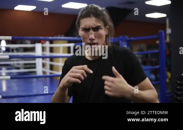 Aggressive long haired man training near boxing ring in modern gym ...