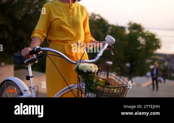 Smiling brunette woman in a long yellow dress standing by her city ...