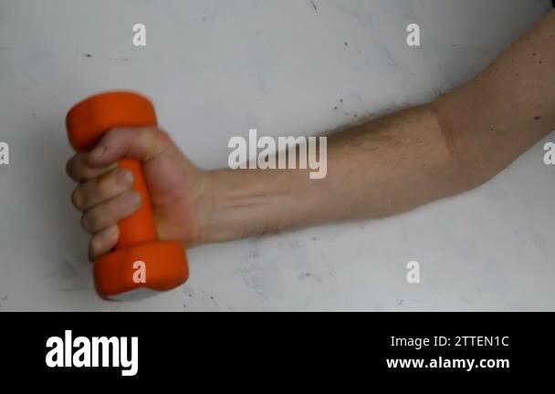 Weak, without muscles male arm does an exercise with a orange dumbbell ...