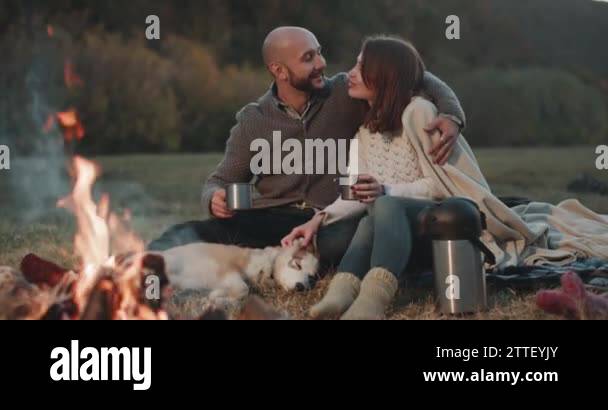 Campfire time for a charismatic young couple with a nice husky dog in the evening they spending ...