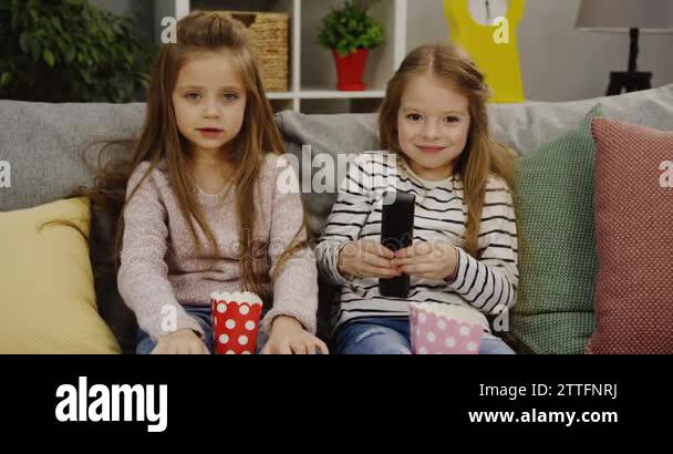 Two cute small girls watching TV and laughing while sitting on the ...