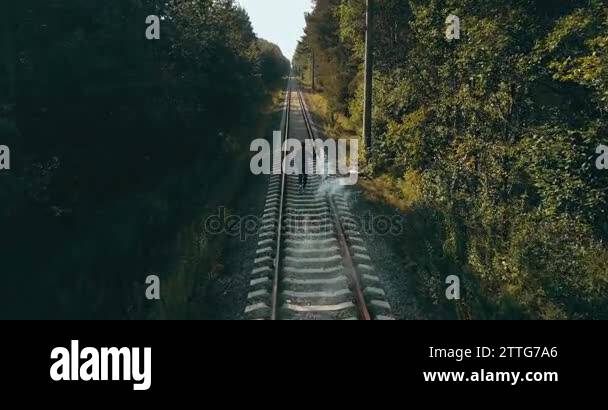 Man running on train tracks with smoke bomb. Drone back view. Runner signaling to oncoming train ...