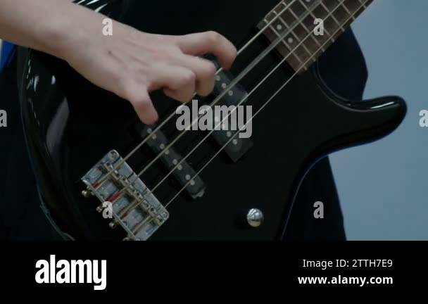 Close-up of the fingers of a teenager playing a black electric bass ...