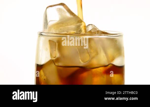 Extreme close up of pouring carbonated cola soft drink in transparent glass with ice cubes until ...