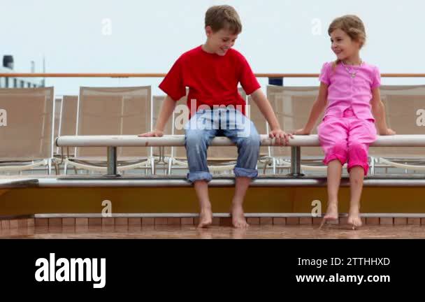 Two kids boy and little girl sit at pool edge near deckchairs Stock ...