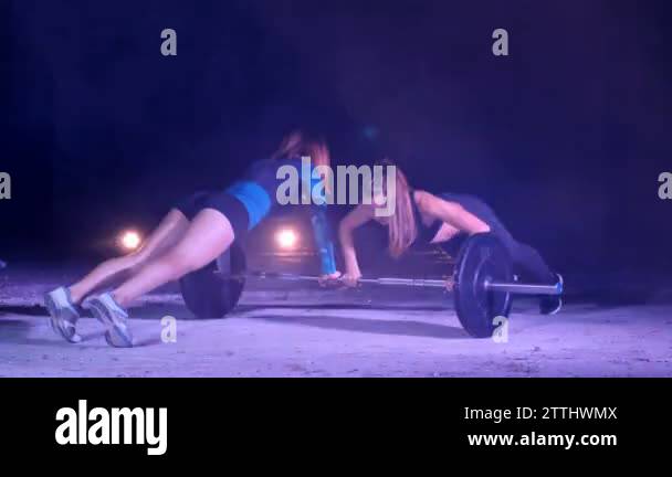Two Athletic Girls In Pair Doing Various Strength Exercises With A Barbell Push Ups At Night