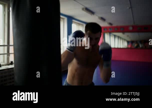 Muscular male professional boxer trains by punching bag at the gym in ...