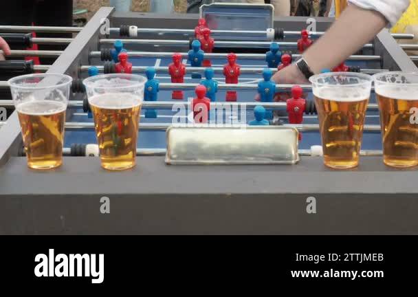 Young people play table football and drink beer outdoors. Figures of ...