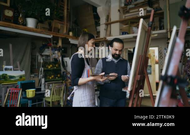 Smiling artist man teaching young girl to draw paintings and explaining ...