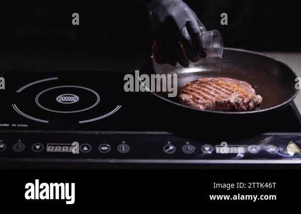 Unrecognized cook pours alcohol on big steak lying on the pan close up ...