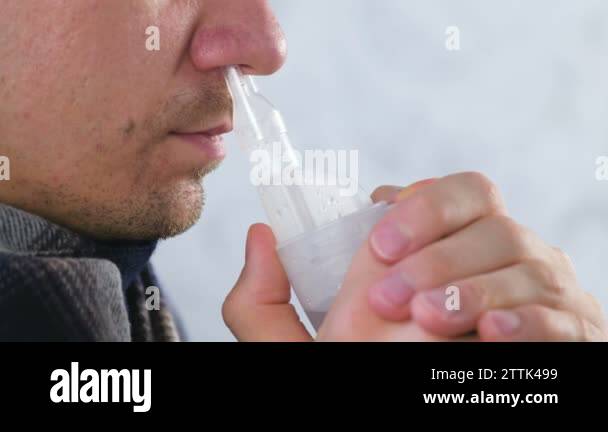 Sick man inhaling through inhaler nozzle for nose. Close-up nose, side ...
