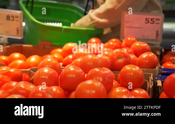 Young guy chooses tomatoes in a supermarket. A hand takes a red tomato ...