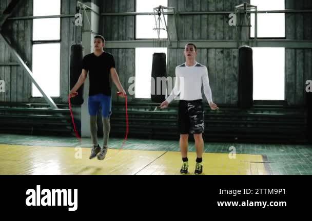 Young boxers in casual clothes jumping using a jump rope while warming ...