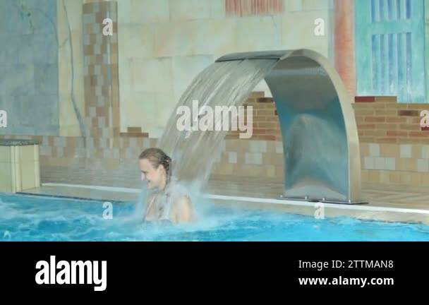 Girl playing in a swimming pool standing under a jet of water from a ...