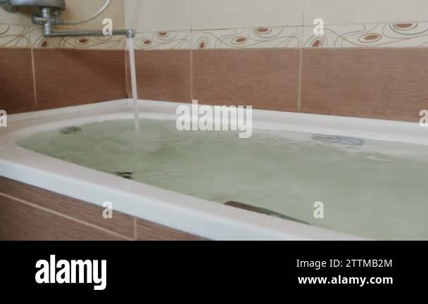 Water flows from the faucet into the tub. Tub filled to the brim with ...