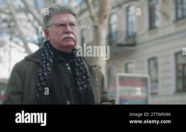 Stout old man with a mustache walking along a historic street in slow ...
