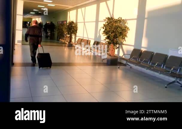 Back view of passenger walking and carrying a suit case in an airport ...