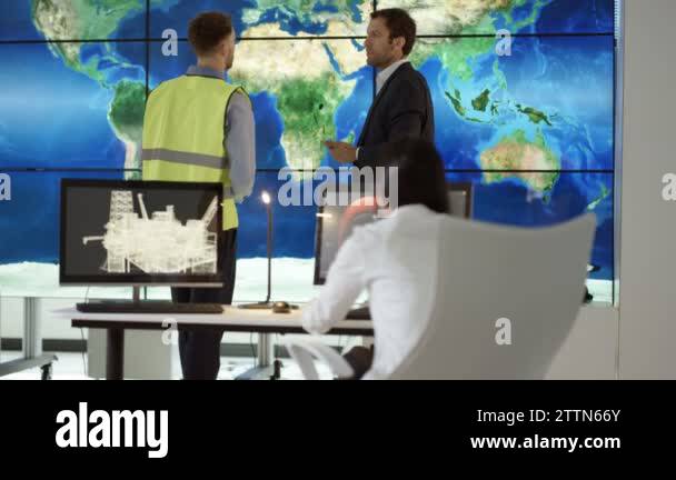 4K Engineering team in discussion looking at large world map graphic on ...