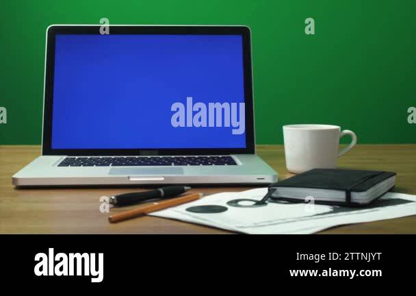 Laptop with a green screen and black notepad on table. Green screen ...