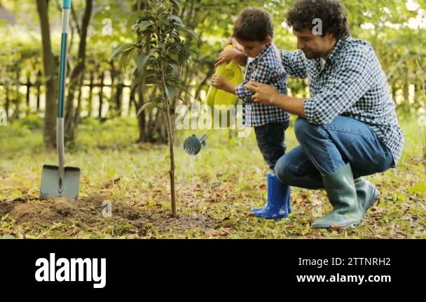 Portrait of a boy and his dad watering a tree. Dad helps his son. Happy ...