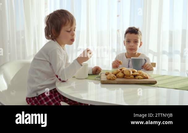 Two boys having breakfast in modern kitchen. Boy eat cookie with milk ...