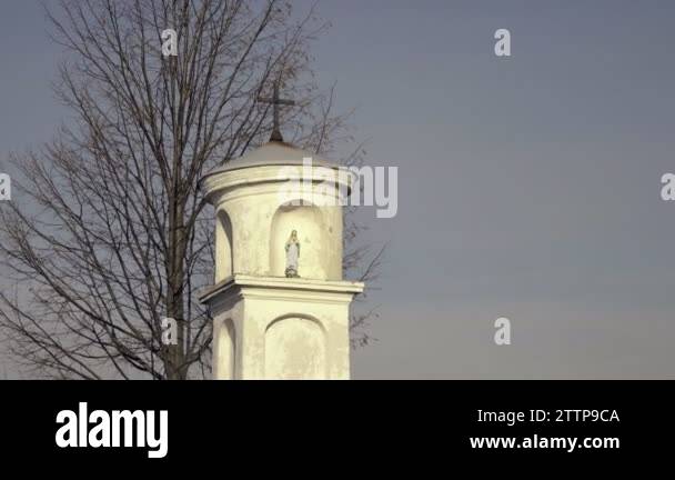 Statue of Virgin Mary with Jesus. Small Christian cross with sculpture, blue sky and tree in ...