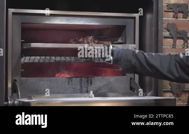 Cook in black rubber gloves puts piece of meat in oven with fire using ...