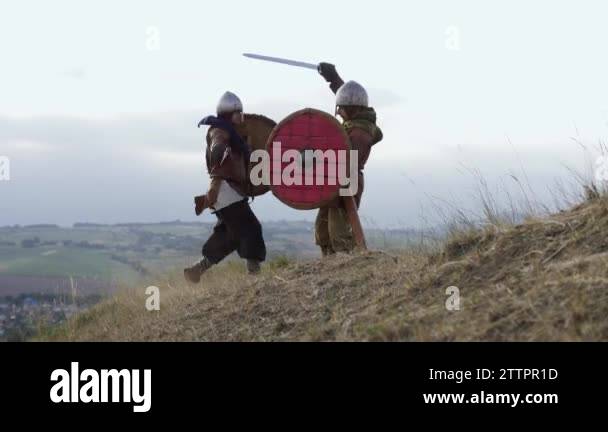 Two warriors Viking are fighting with swords and shields in the meadow ...