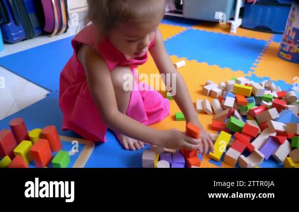 Little Asian cute girl playing cubes, sitting on a color floor. The ...