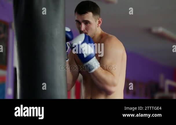 Muscular male professional boxer trains by punching bag at the gym in ...