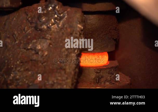 Some blacksmith puts a burned iron ingot under a press using metal ...