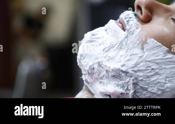 Barbershop client with white shaving cream on face.Young black man with ...
