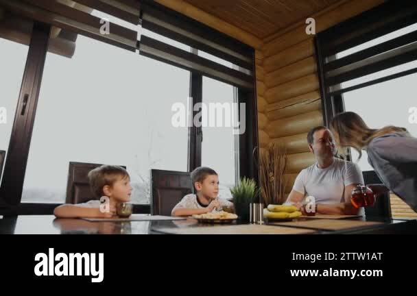 Family of four having Breakfast in his kitchen with large Windows. People are smiling, mother ...