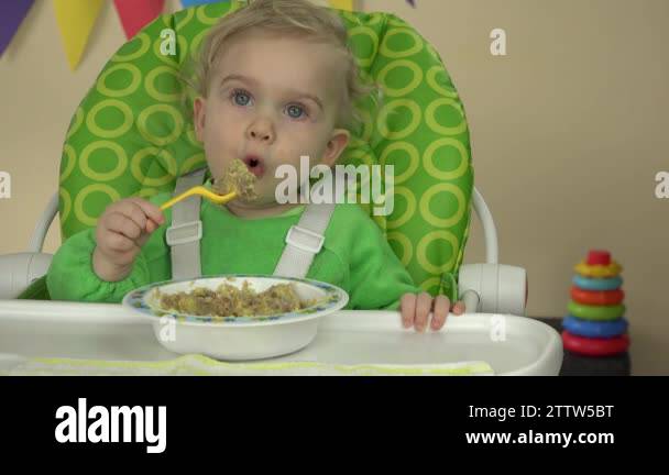 little girl practice eat gruel with spoon sit on baby chair. 4K Stock ...