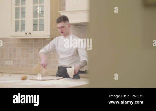 Attractive guy spinning and tossing two disks of pizza dough in kitchen ...