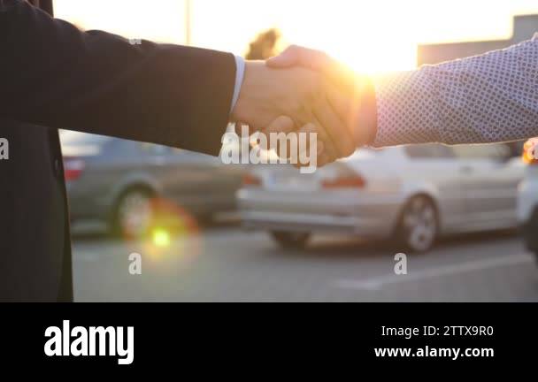 Two businessmen shaking hands of each other with cars in parking at ...